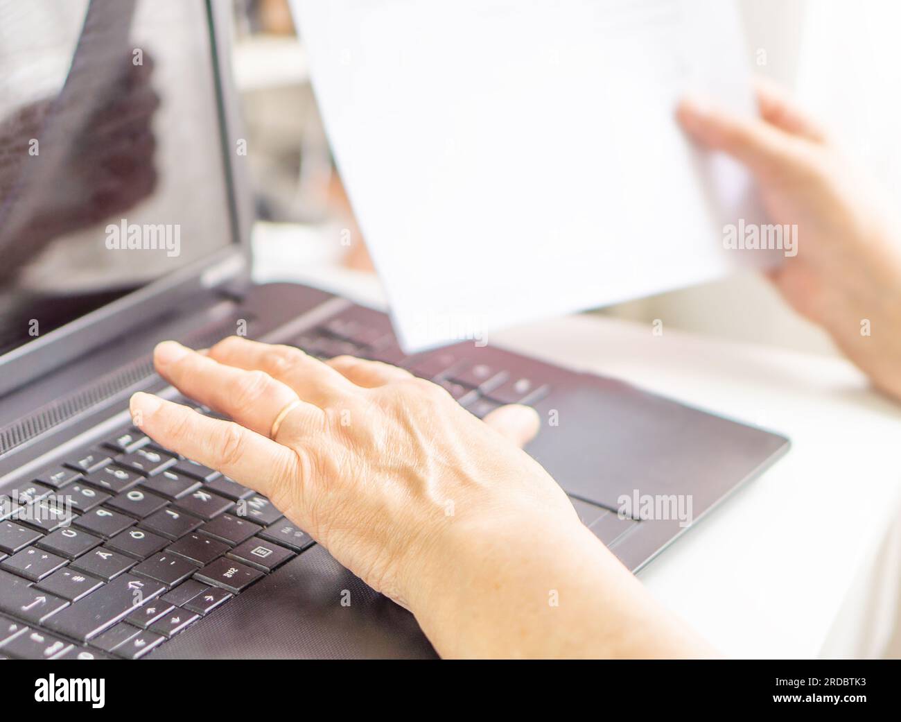 Close up of middle aged female hands with laptop and paper document ...