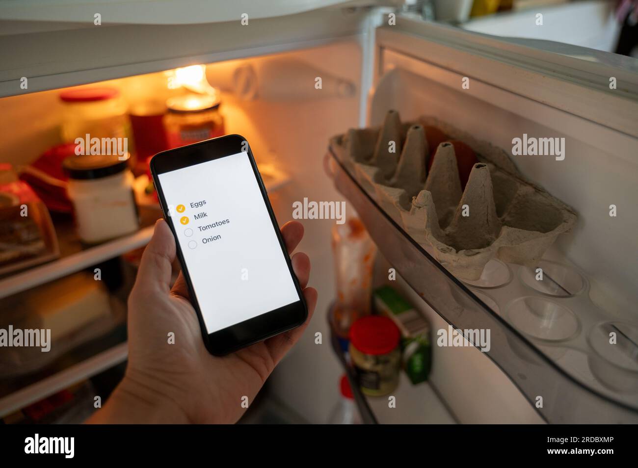 Person with smartphone in hand, making shopping list with opened fridge ...