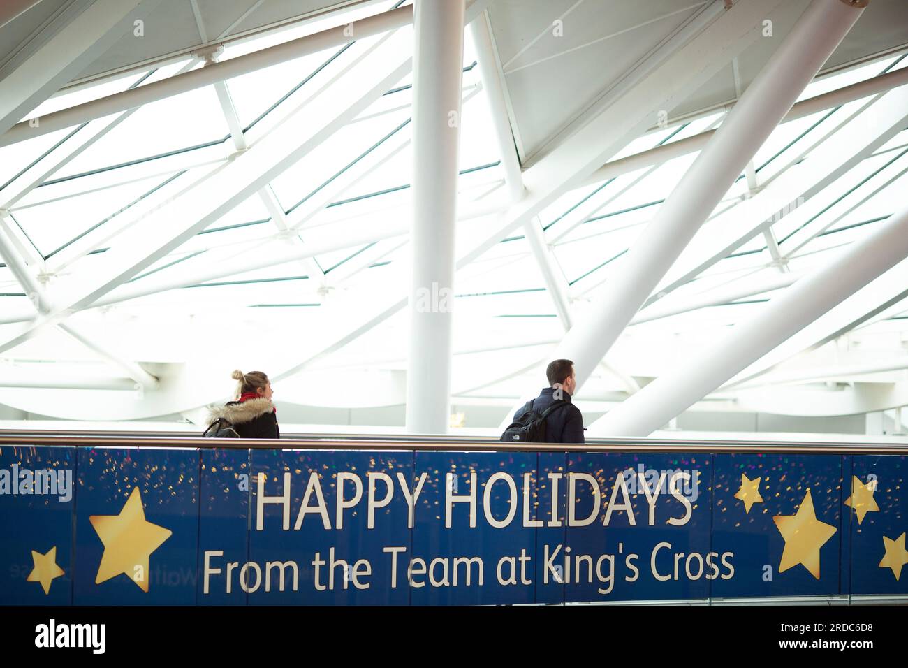 Passengers walk behind a banner reading ‘Happy Holidays’ at King Cross ...
