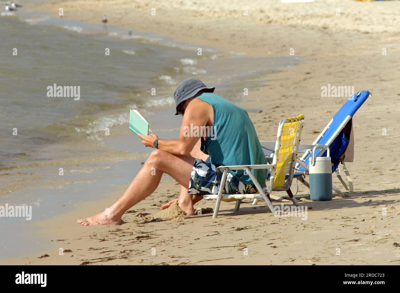 Man holding a book playfully covers his foot with sand while enjoying ...