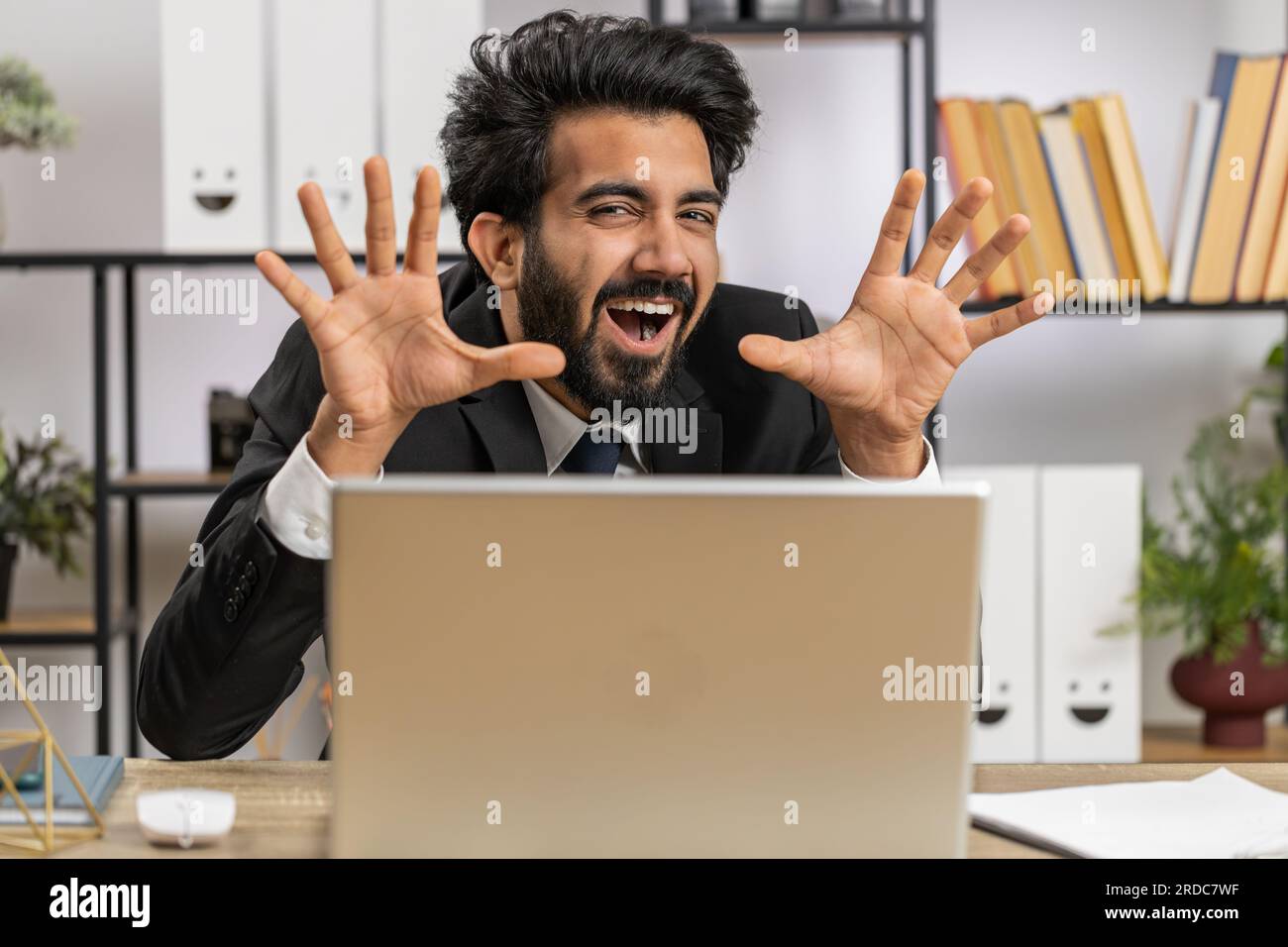 Indian businessman hiding behind laptop computer, making funny face ...