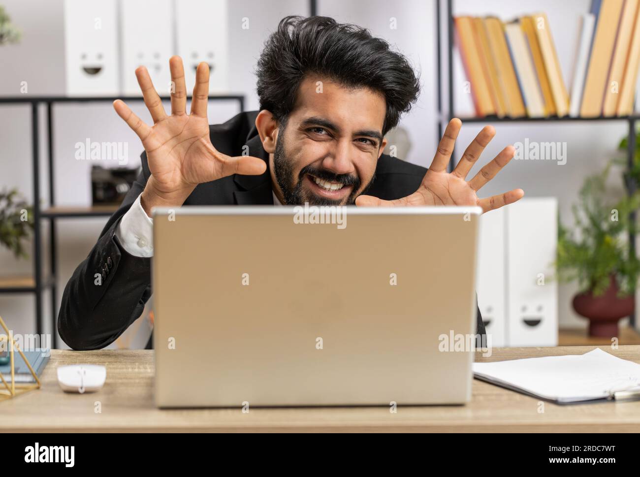 Indian businessman hiding behind laptop computer, making funny face ...