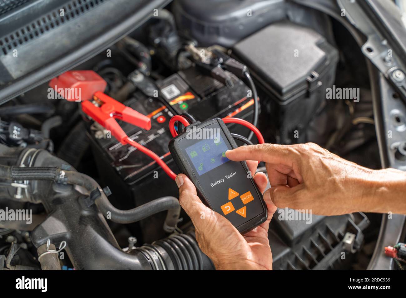 Close up hands of a male auto mechanic using a battery tester to check ...