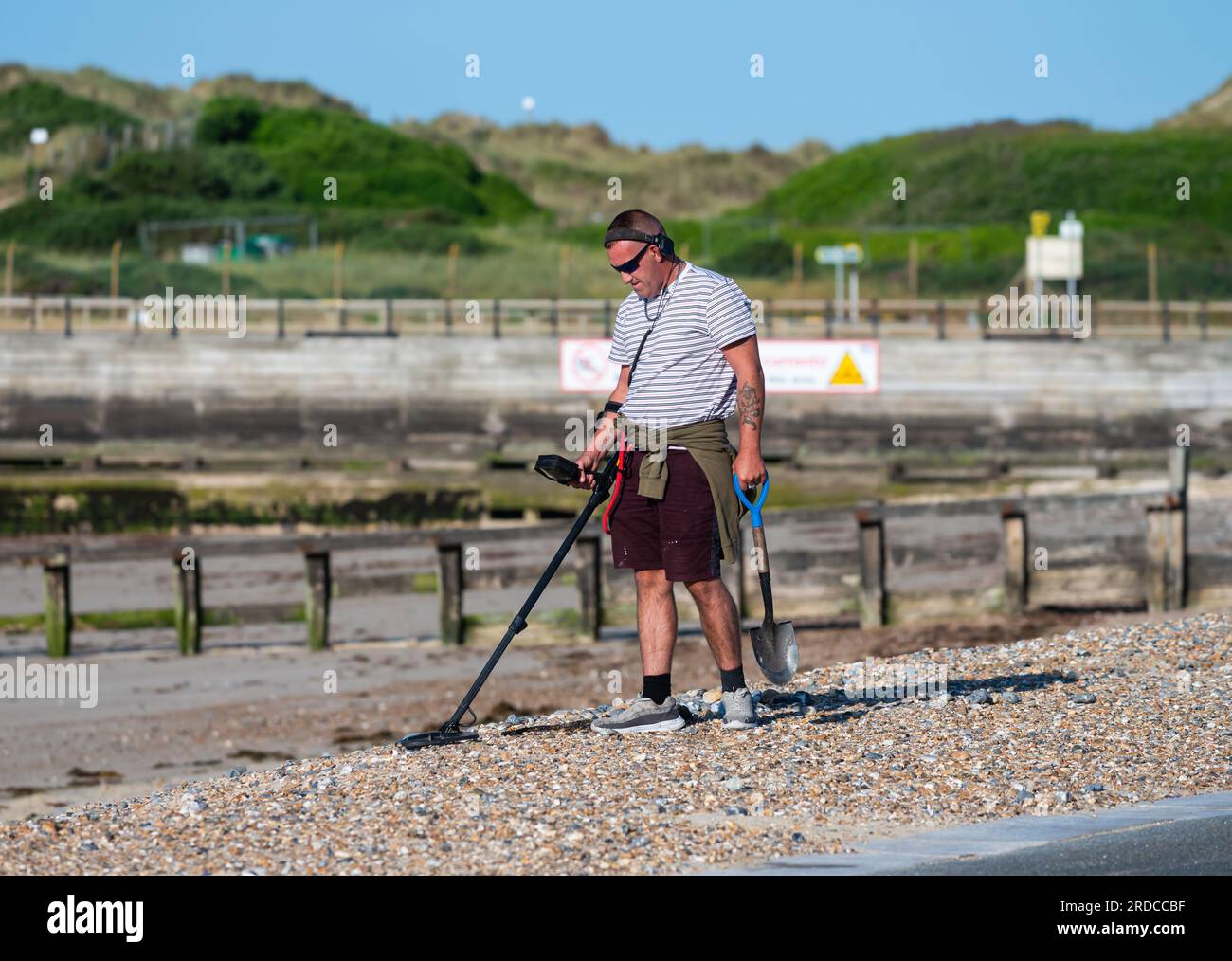 Man on shingle beach with metal detector searching for lost or valuable ...
