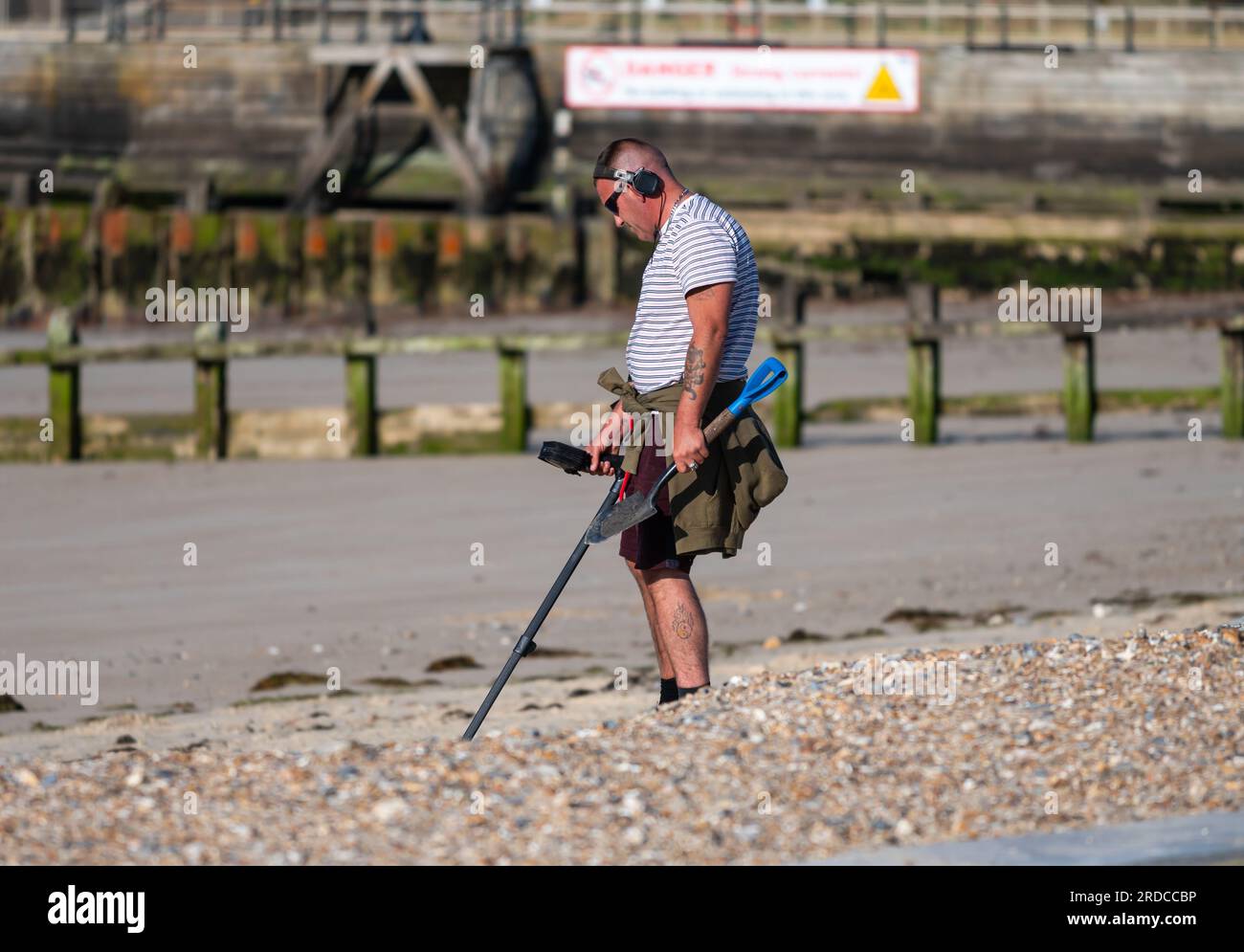 Man on shingle beach with metal detector searching for lost or valuable ...
