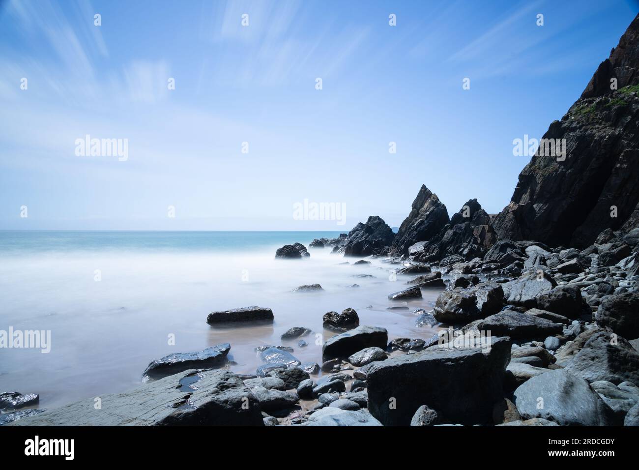 Dark black rocks and cliff with shallow swirling water. Long exposure ...