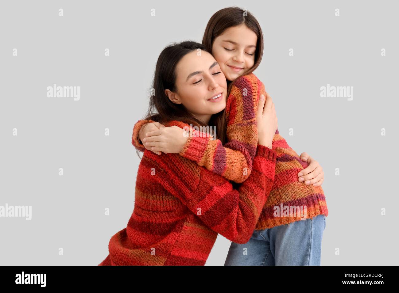 Little girl and her mother in warm sweaters hugging on grey background ...