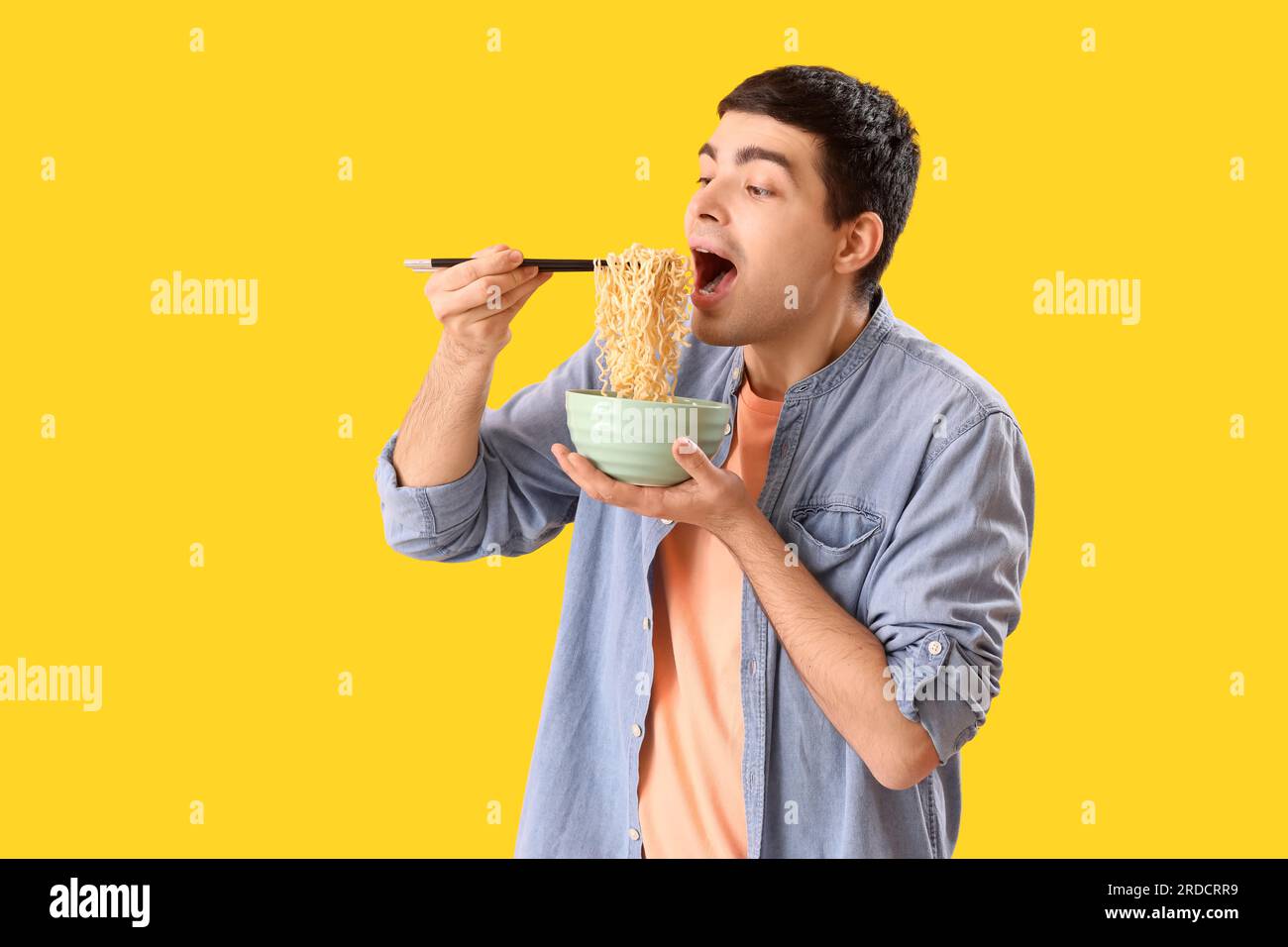 Young man eating Chinese noodles on yellow background Stock Photo - Alamy