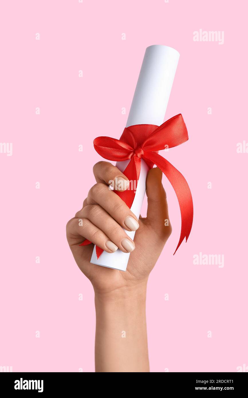 Woman holding diploma with ribbon on pink background Stock Photo - Alamy