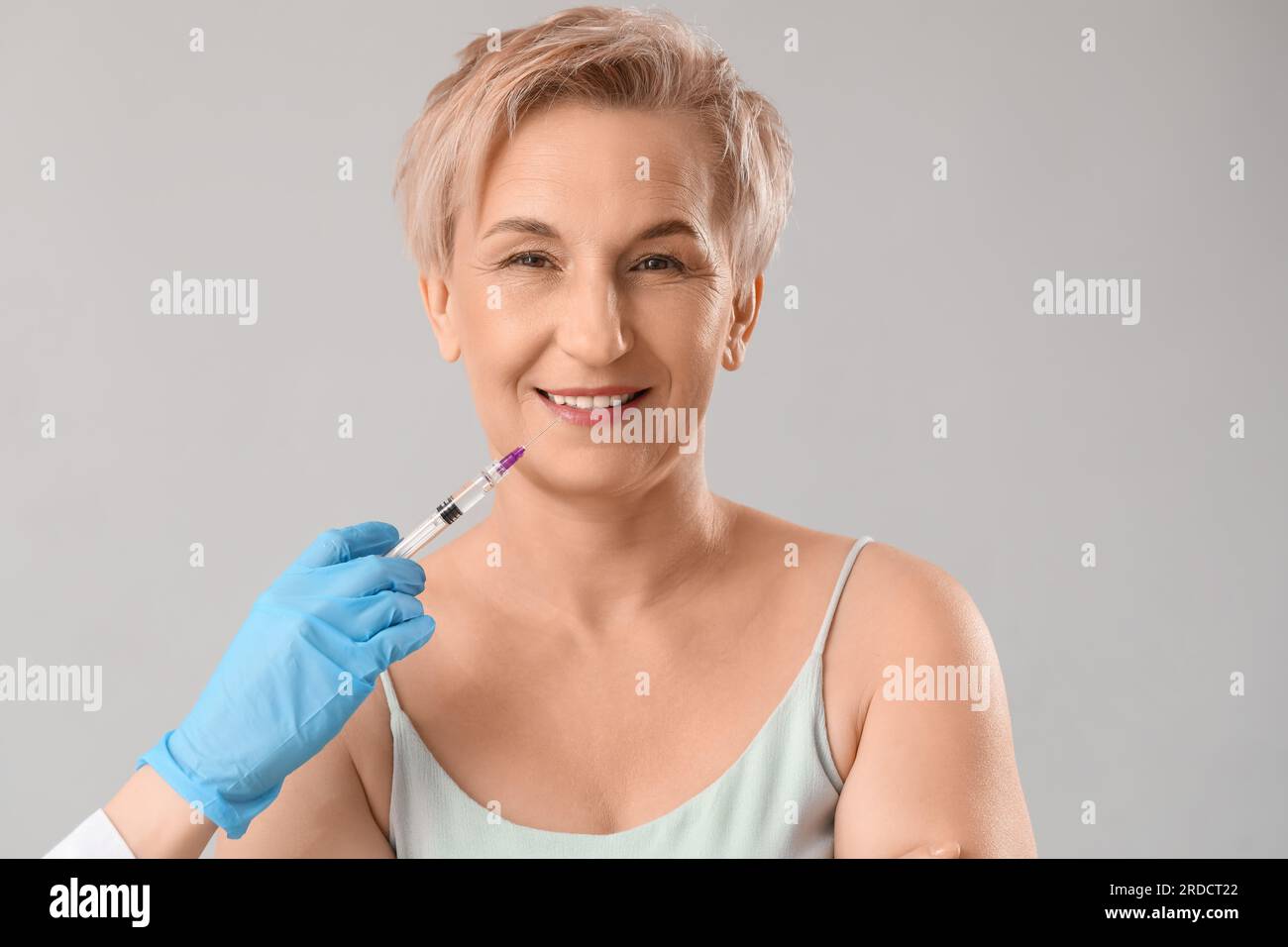 Mature woman receiving filler injection on light background Stock Photo ...