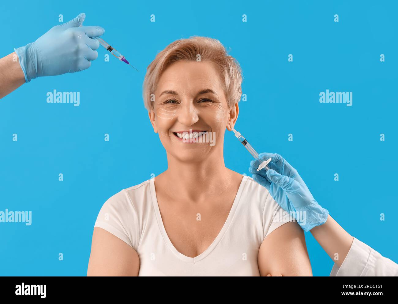 Mature woman and beauticians hands with filler injections on blue ...