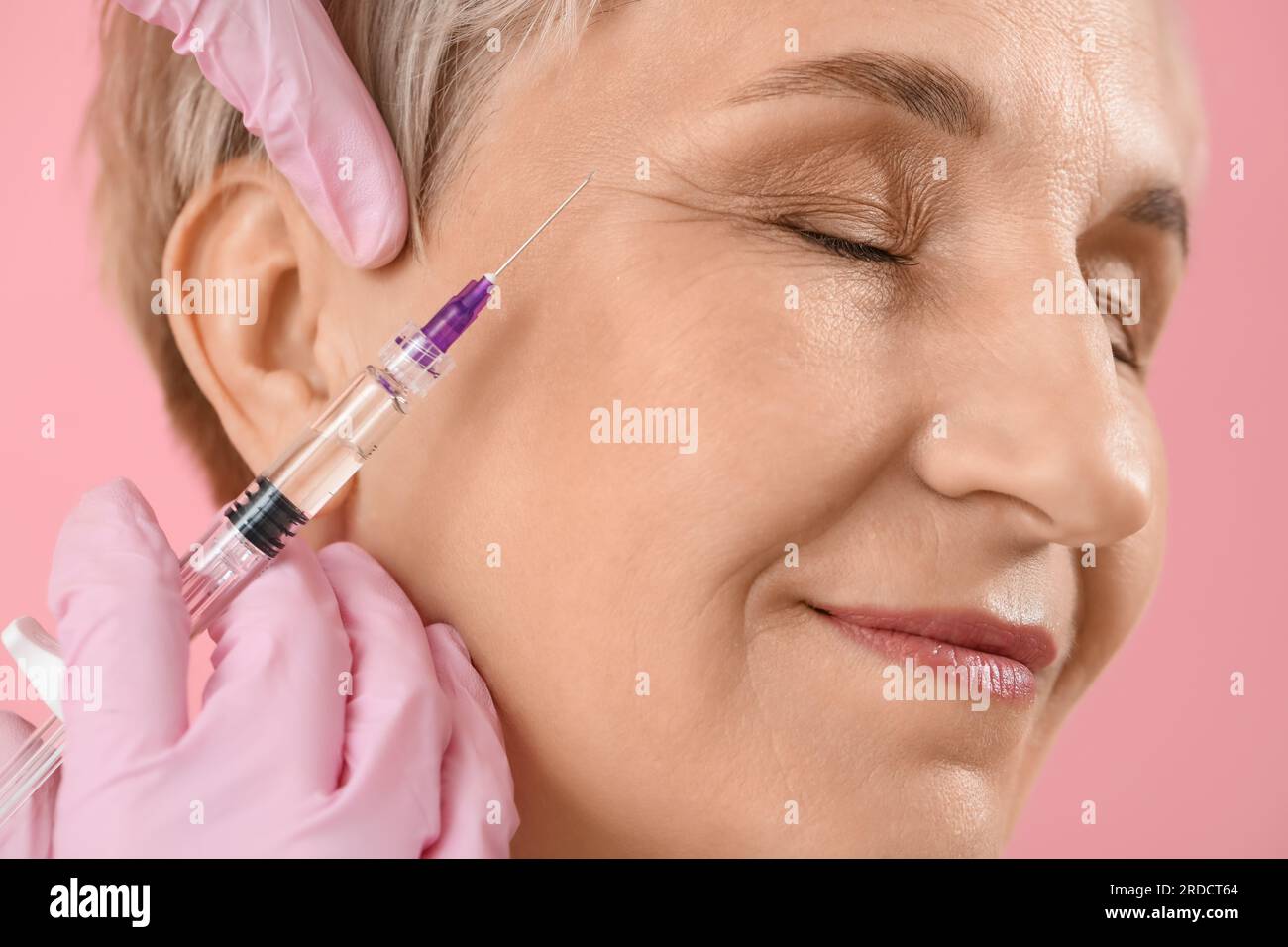 Mature woman receiving filler injection on pink background, closeup ...