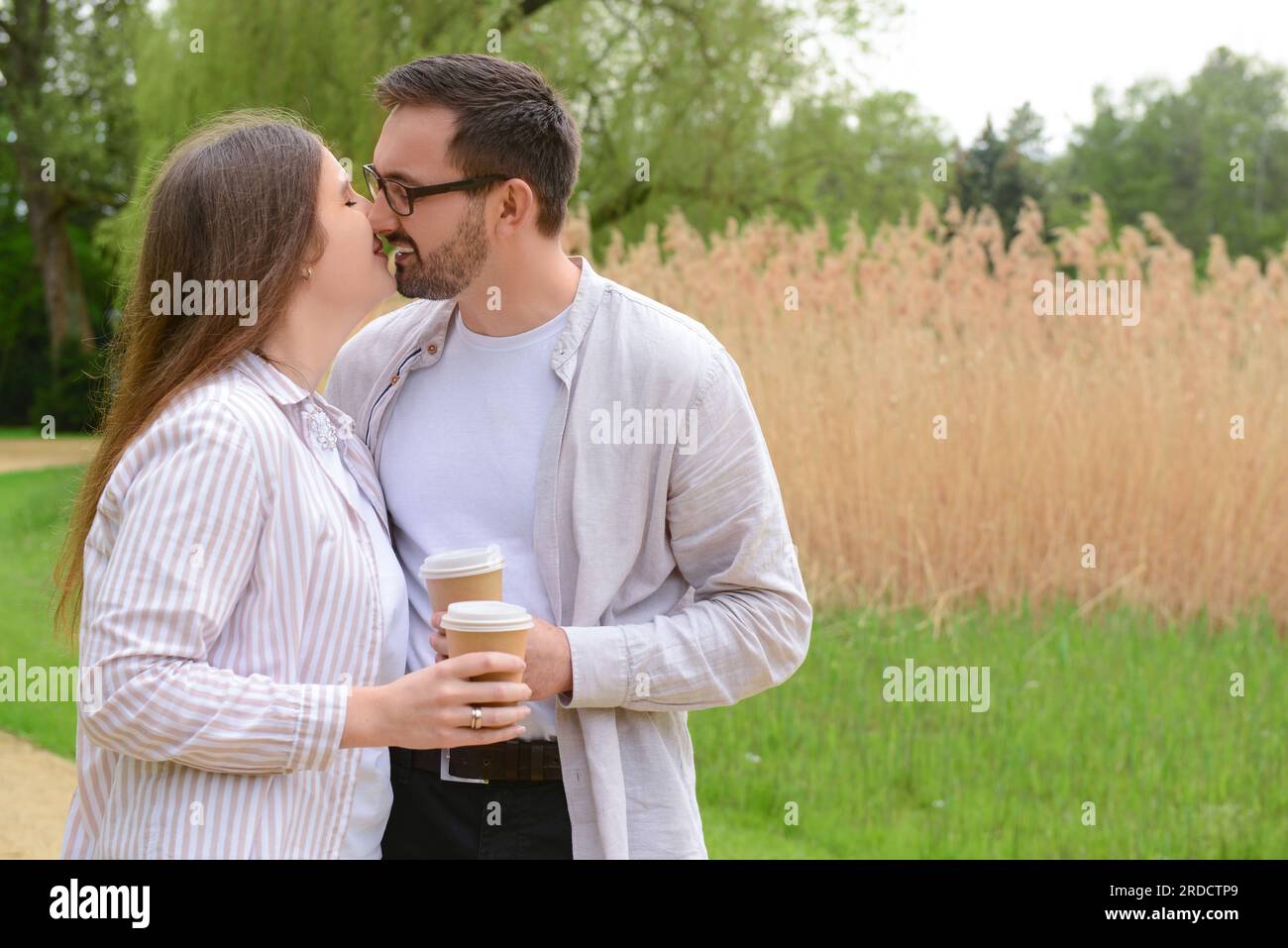 Beautiful happy loving couple kissing in park and drinking coffee on ...