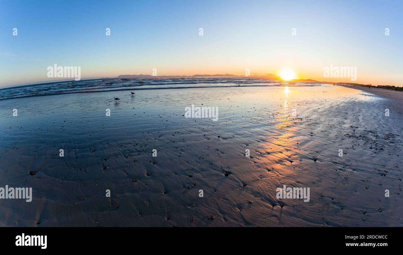 Beach ocean coastline as sun dipping water reflections behind mountains ...