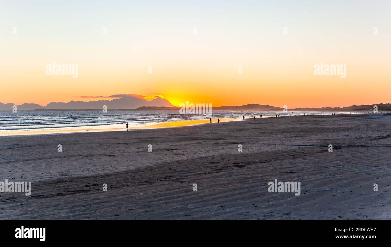 Beach ocean coastline as sun dipping behind mountains with distant ...