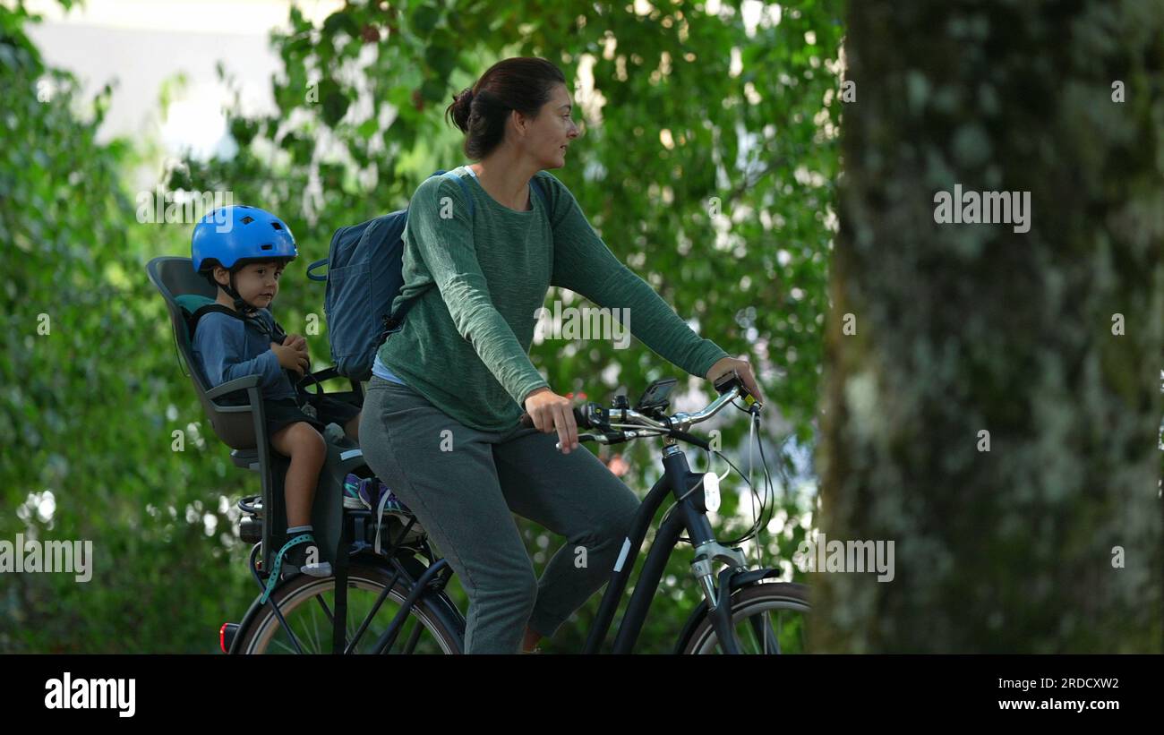 Mother and child riding bicycle kid in bike back seat wearing helmet ...