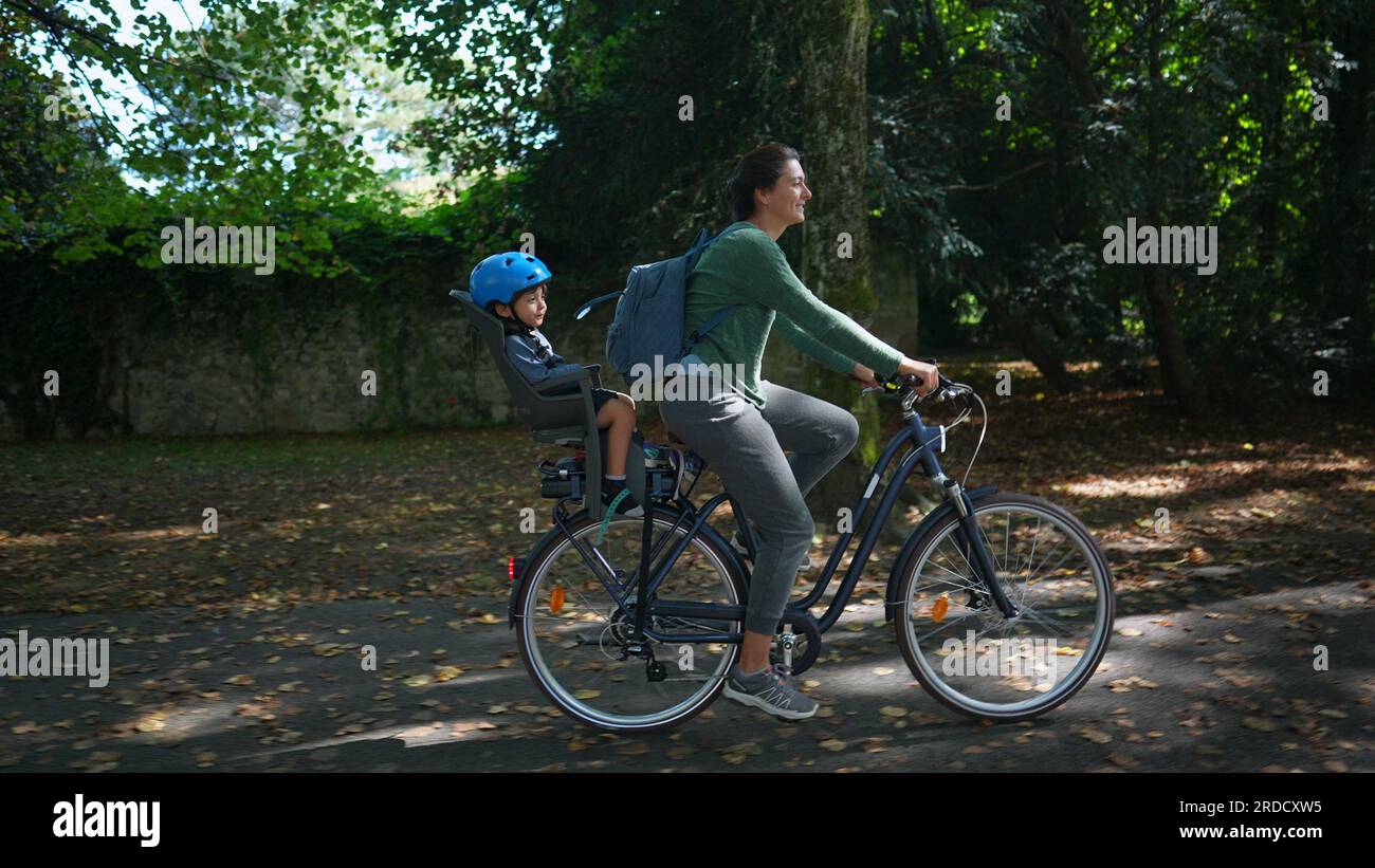 Mother riding bicycle outside at park with kid in back seat Stock Photo ...