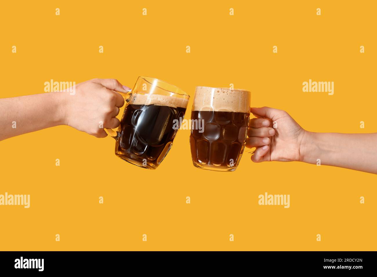 Female hands with mugs of cold beer clinking on yellow background Stock ...