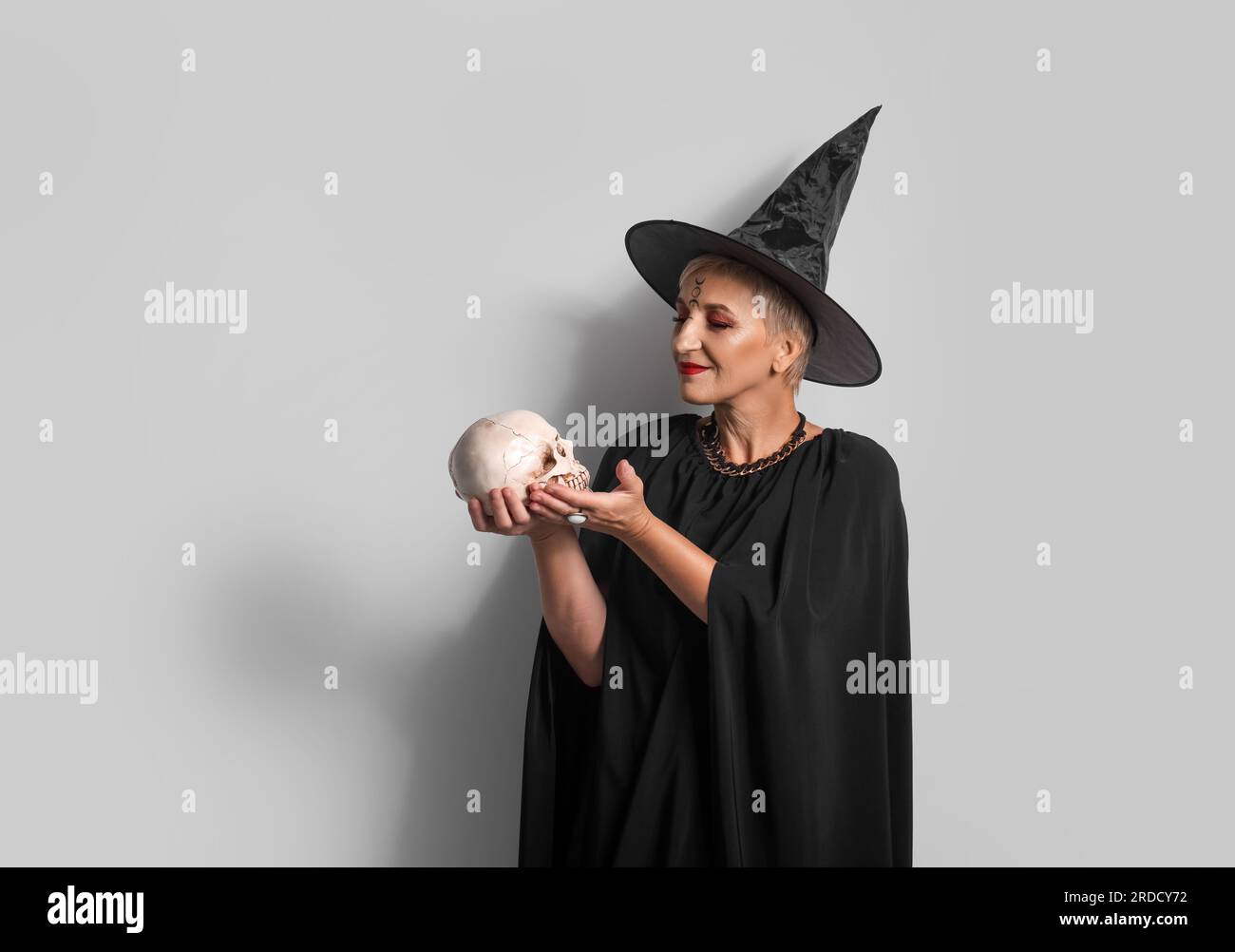 Mature witch with human skull on grey background Stock Photo - Alamy