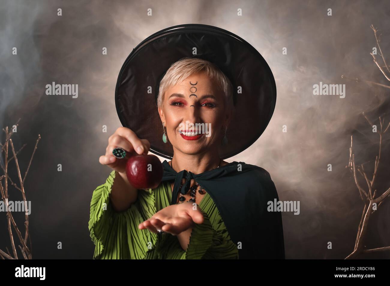 Mature witch with apple and smoke on dark background Stock Photo - Alamy
