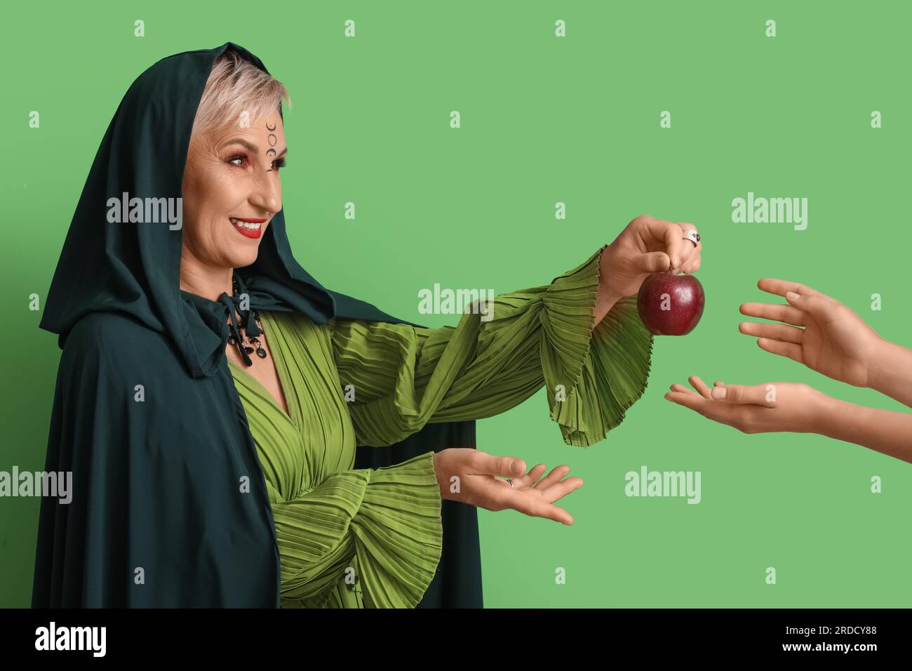 Mature witch giving apple on green background Stock Photo - Alamy