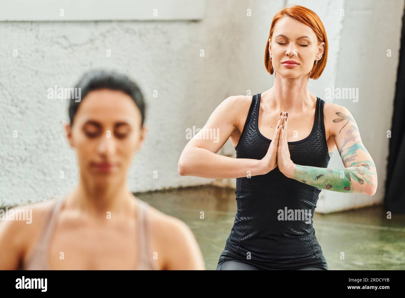 tattooed and redhead woman in sportswear meditating with closed eyes ...