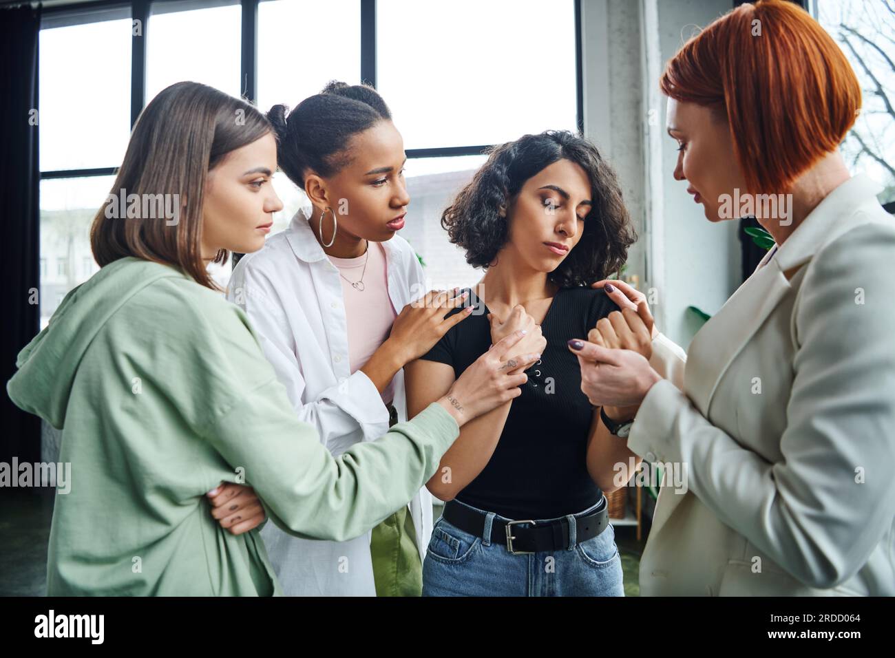 upset multiracial woman standing with closed eyes near multiethnic ...