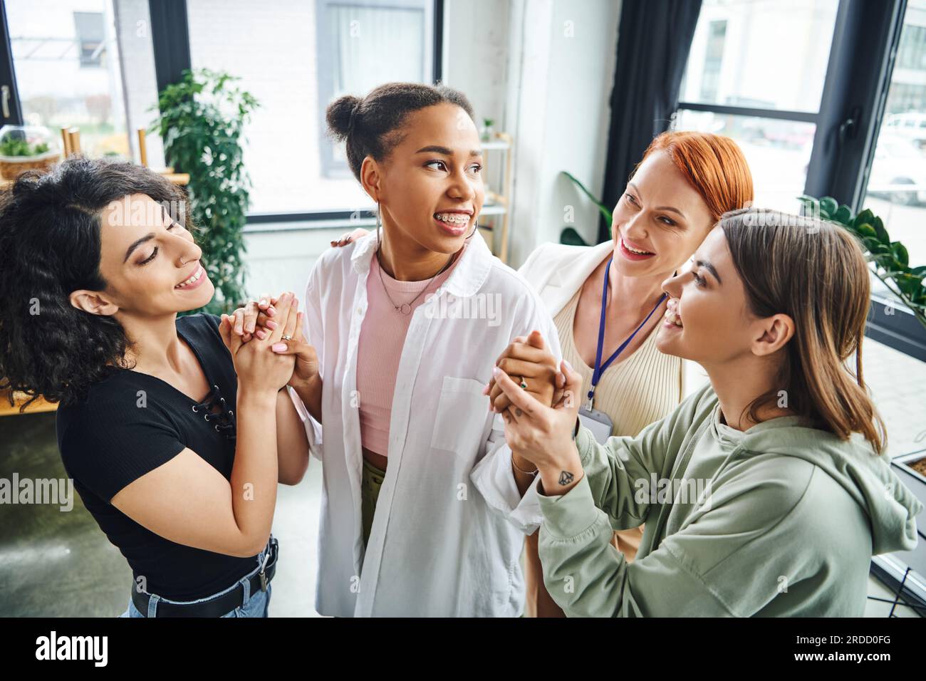 multiethnic friends and smiling motivation coach holding hands of ...