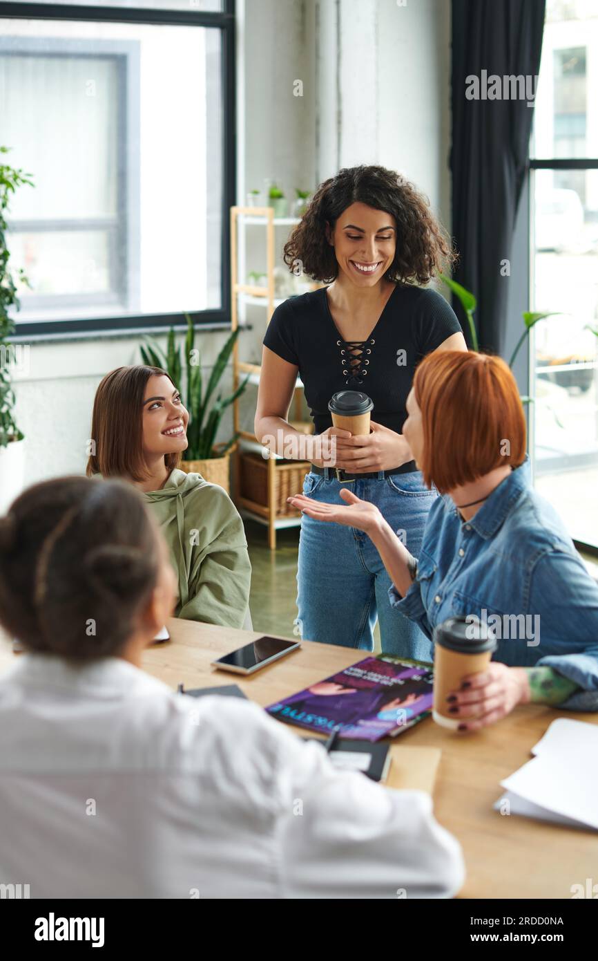 redhead woman pointing at smiling multiracial friend standing with ...