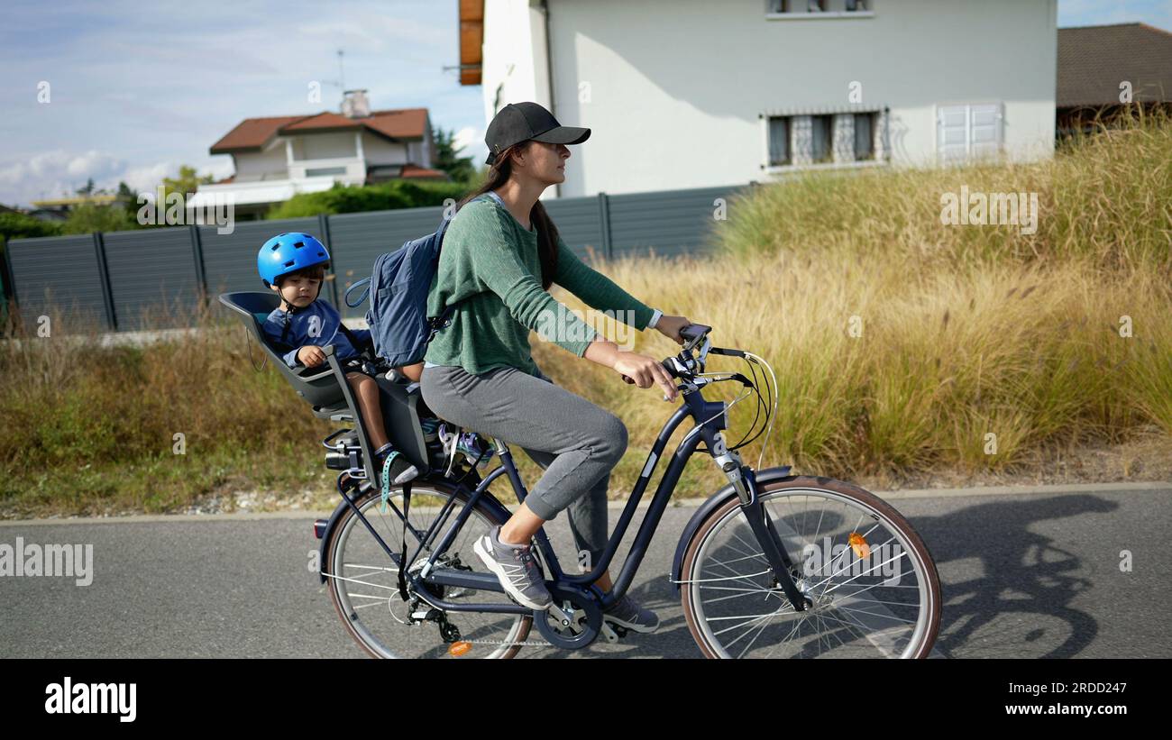 Cyclist mother rides bike outside in green road with child Stock Photo ...