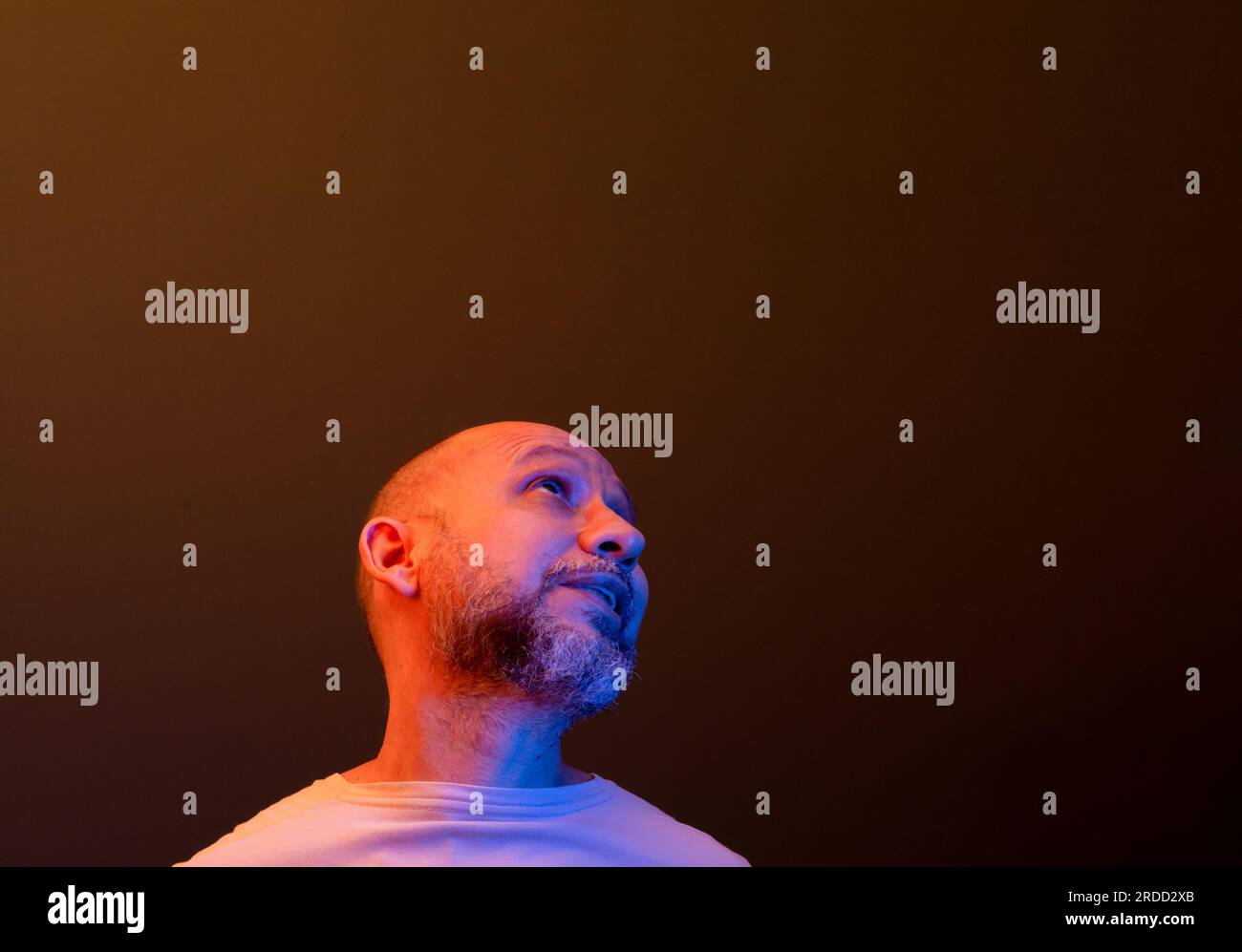 Bald man with beard, serious, looking up with surprised expression. Isolated on dark red ...