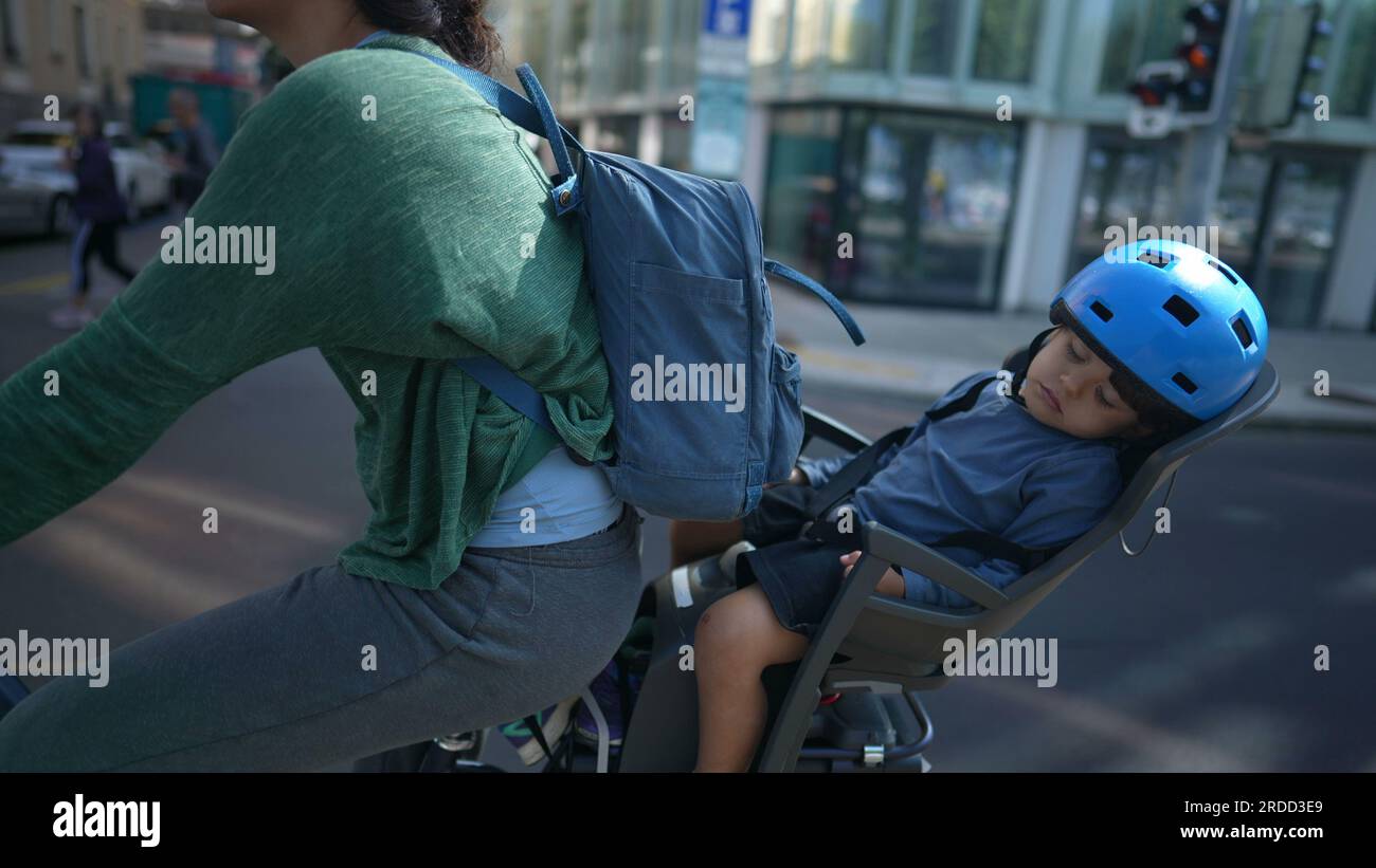 Parent riding bicycle in street with sleeping child in back seat mother ...
