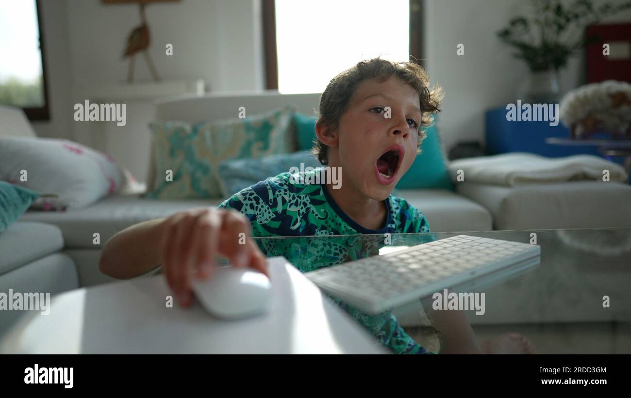 Tired little boy yawning browsing internet online using mouse and ...