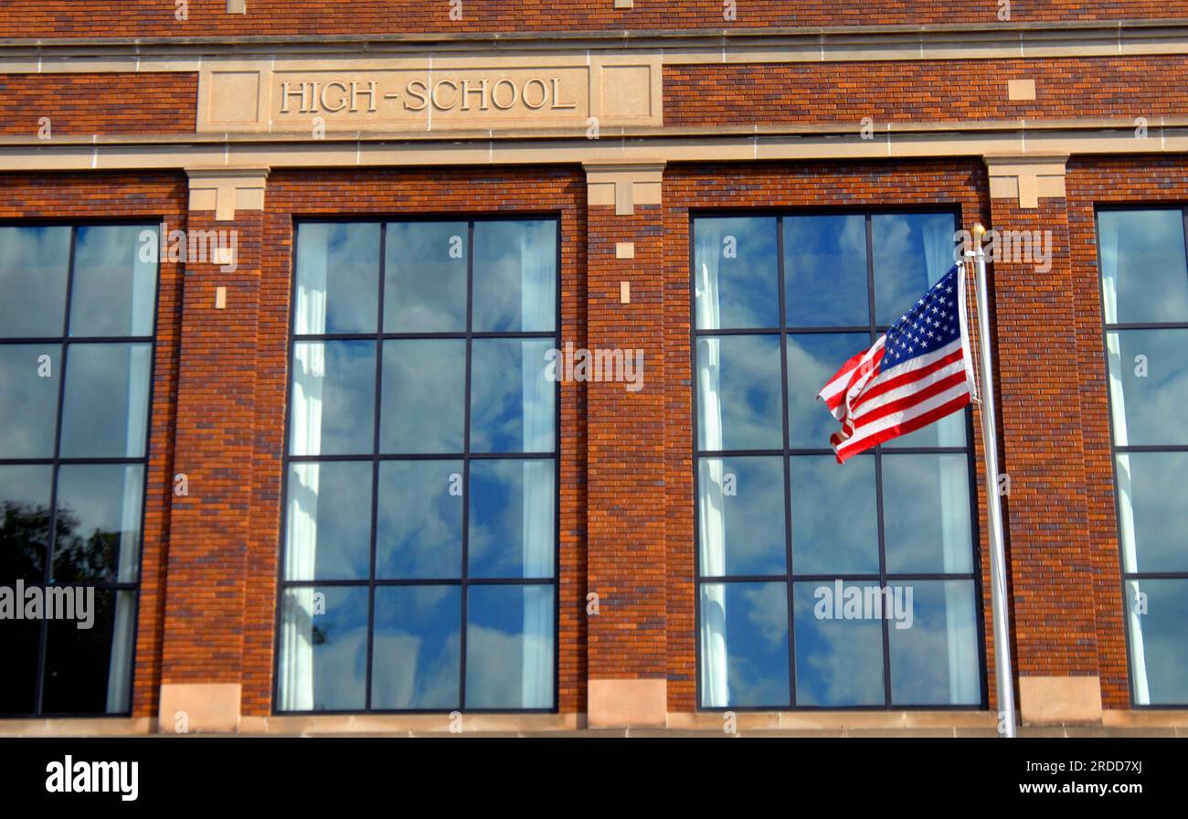 American flag flies in front of a high school building. Windows reflect ...