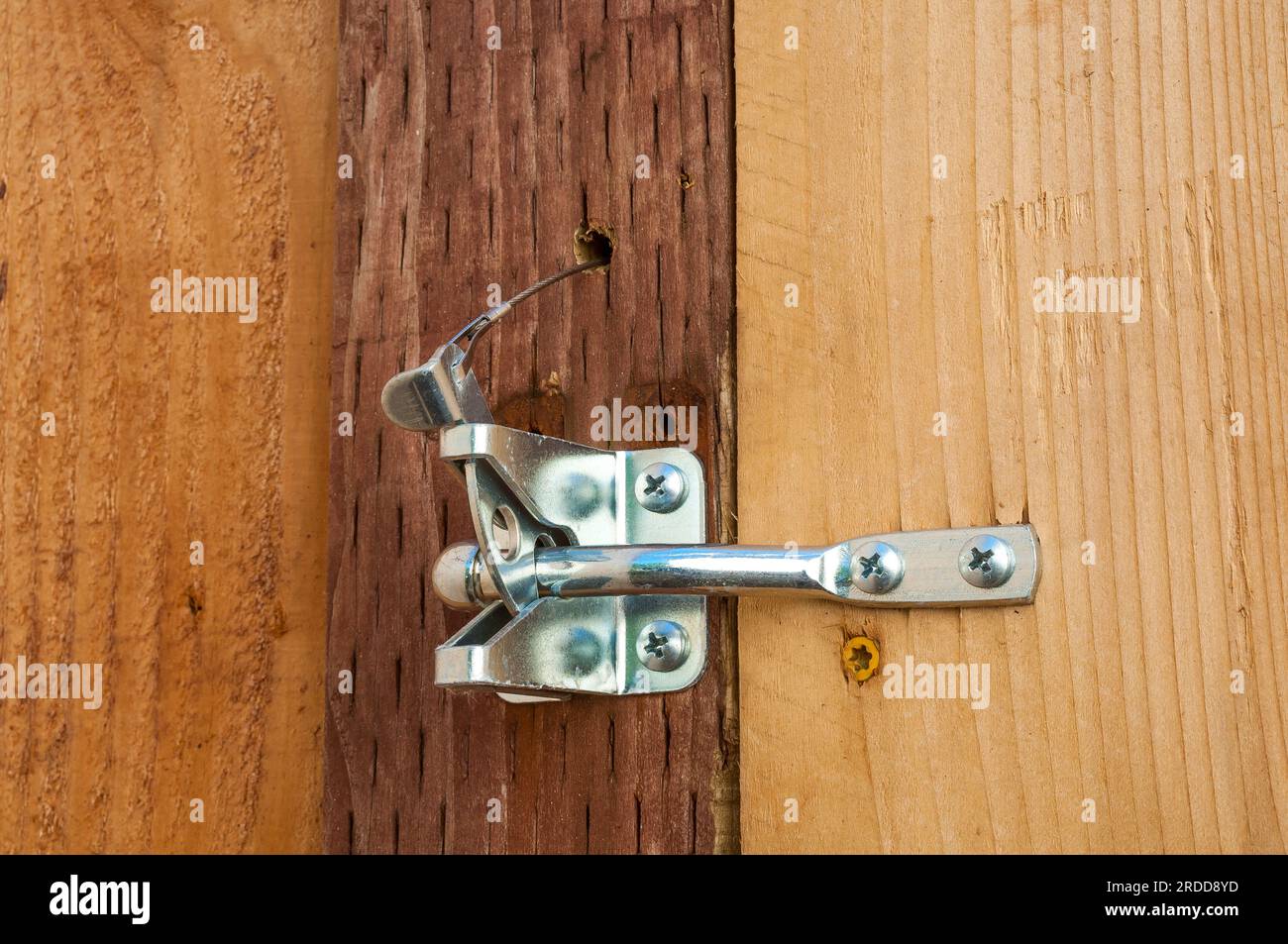 A zinc-coated gate door latch in the closed position, on a wooden fence ...