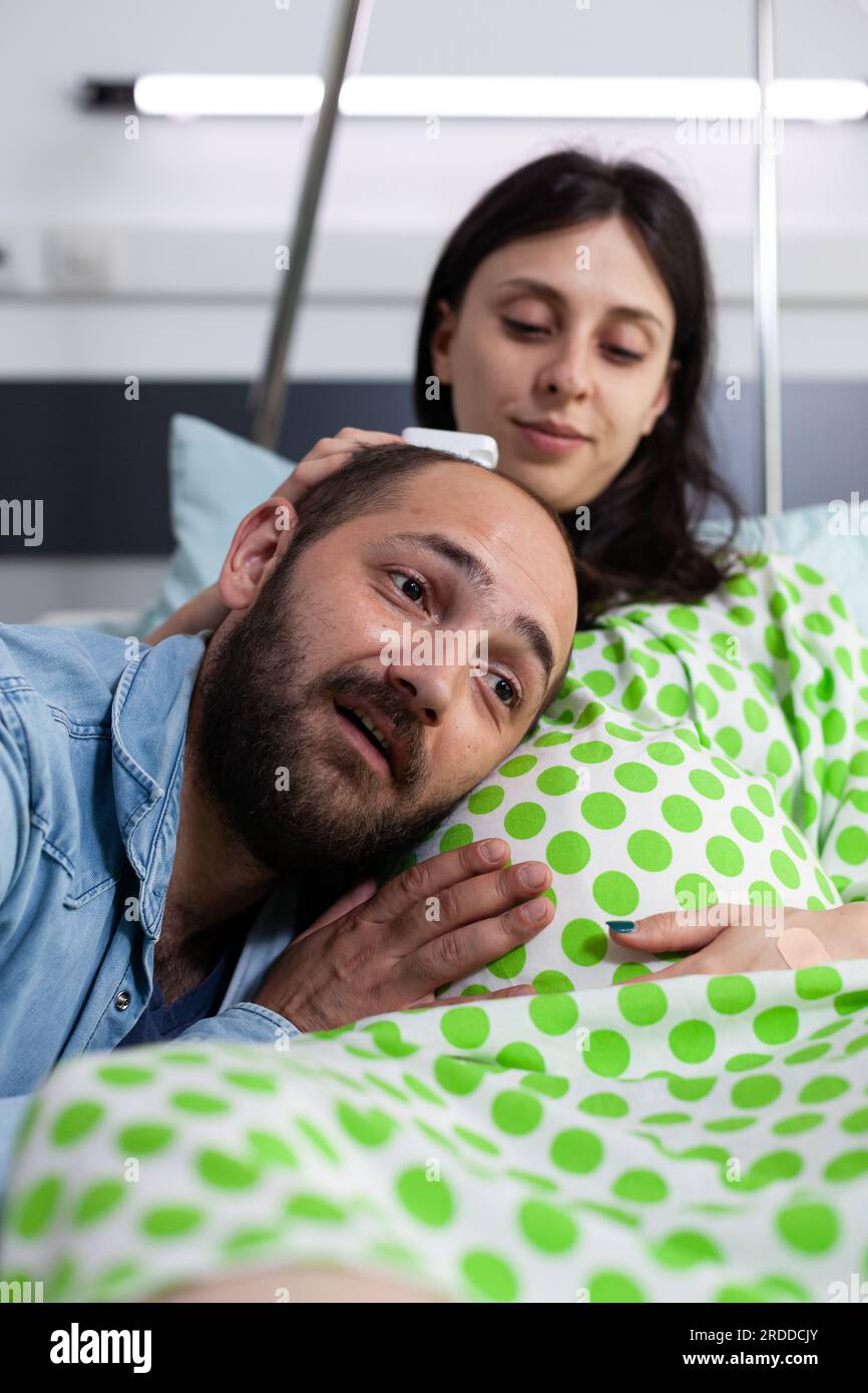 Cheerful future father standing with head on woman belly, talking with ...