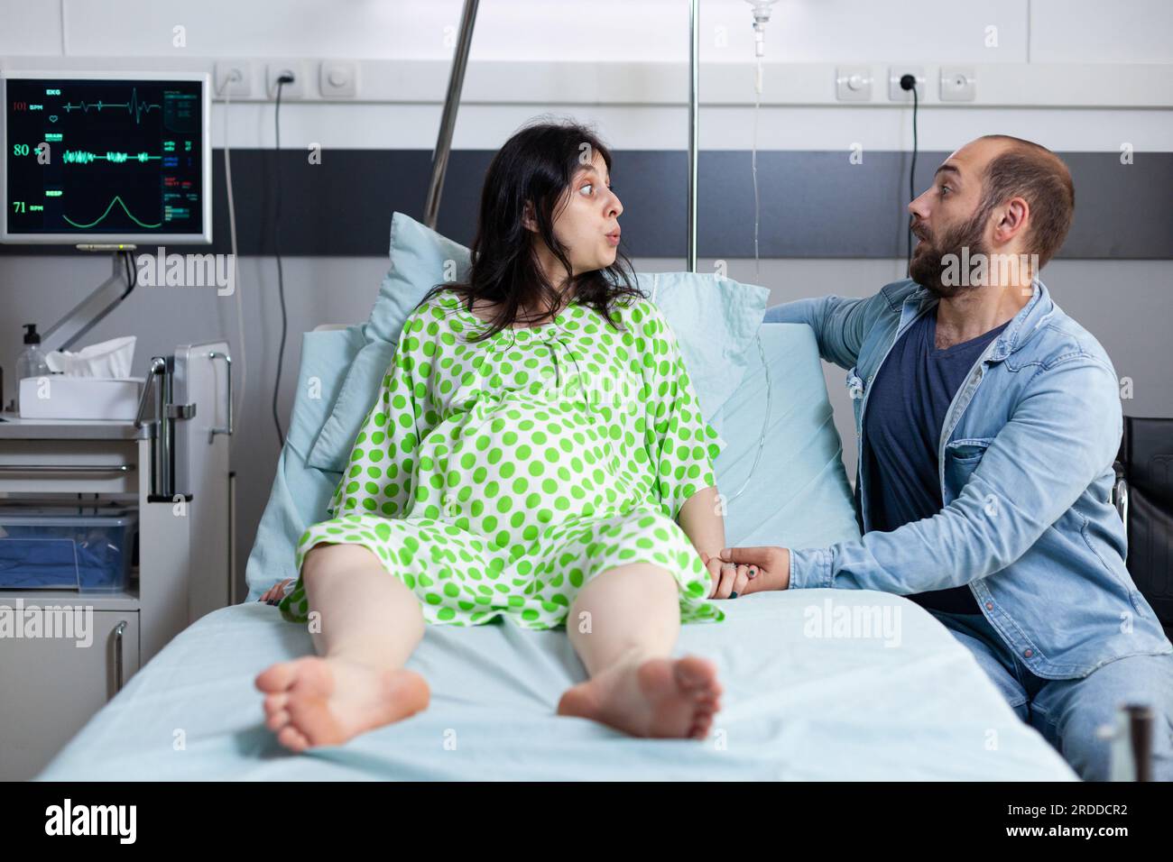 Woman with pregnancy lying in hospital ward bed with husband beside her ...