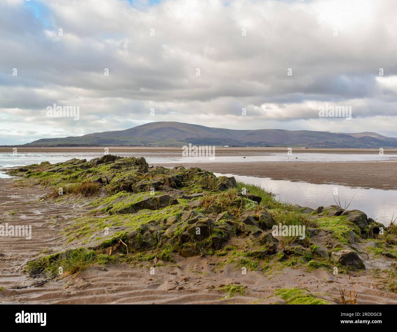 Looking out across a rocky and sandy beach with mountain peaks in the ...