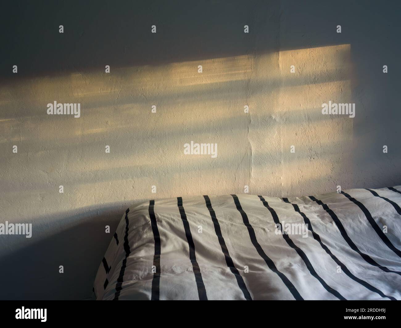 The shadow of a window frame and the light of the sunset above a bed ...