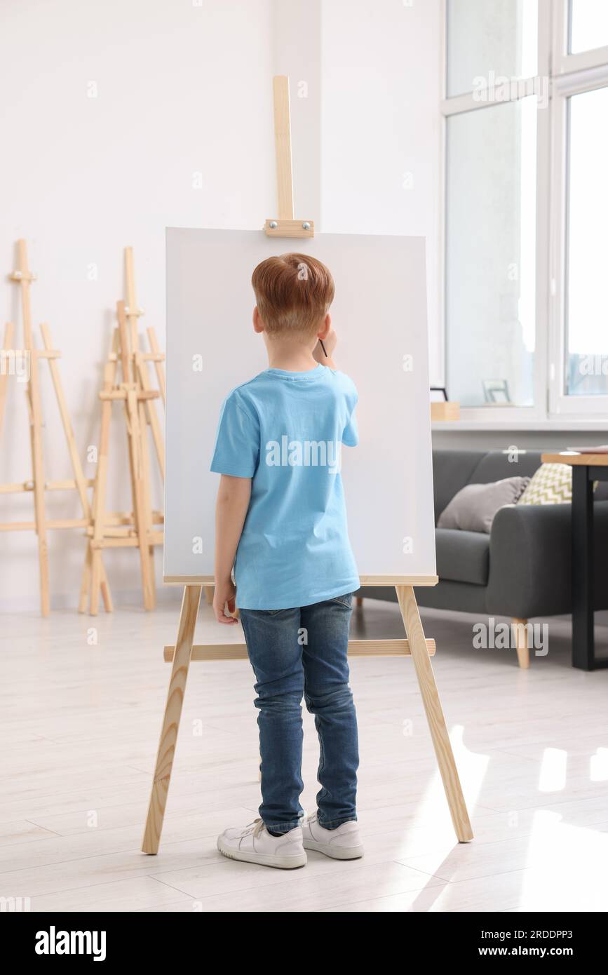 Little boy painting in studio, back view. Using easel to hold canvas ...