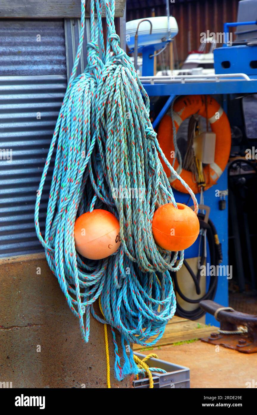 Coiled rope and floats hang on pier next to bright blue fishing boat ...