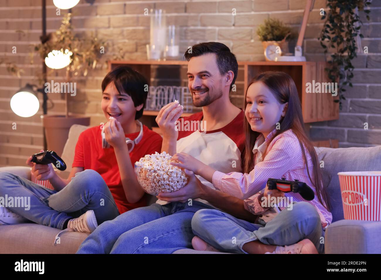 Father with his little children eating popcorn while playing video game ...