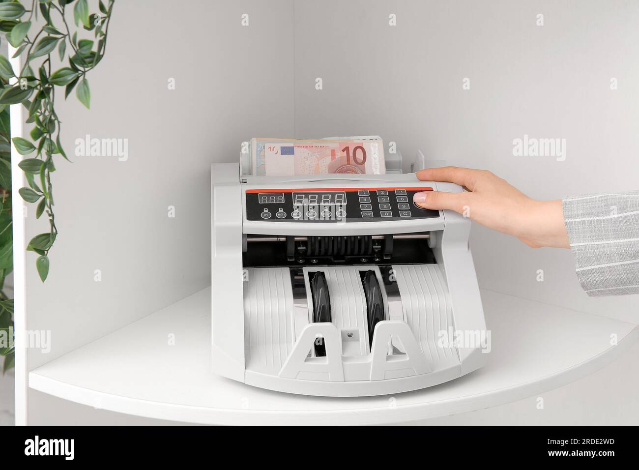 Woman putting euro banknotes into cash counting machine on shelf in ...