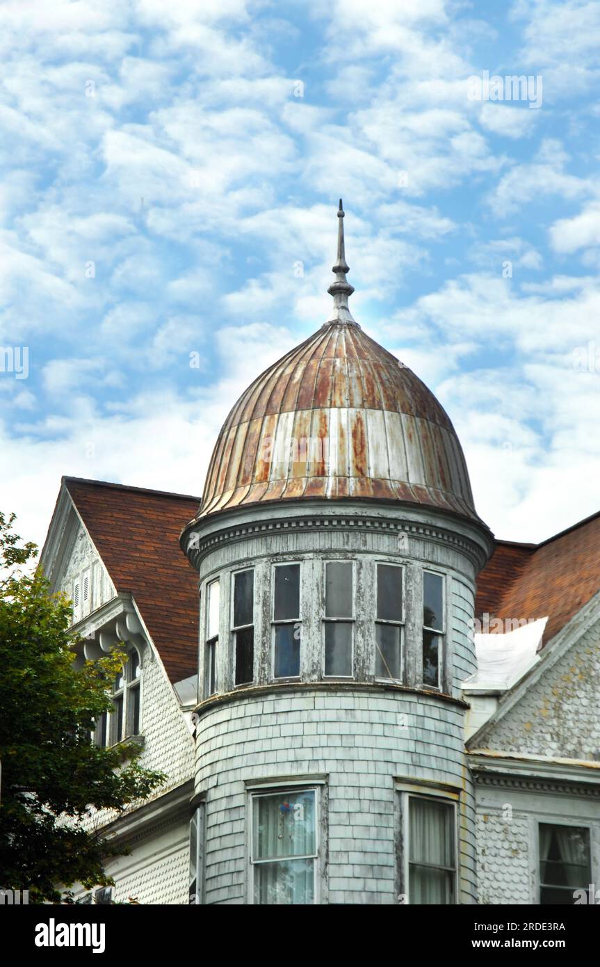 Round tower has domed top and metal finial. Home is white with shingled ...