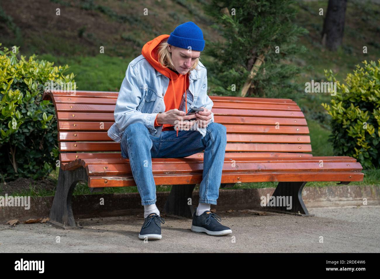 Worried upset young guy sitting alone on bench outdoors with smartphone ...