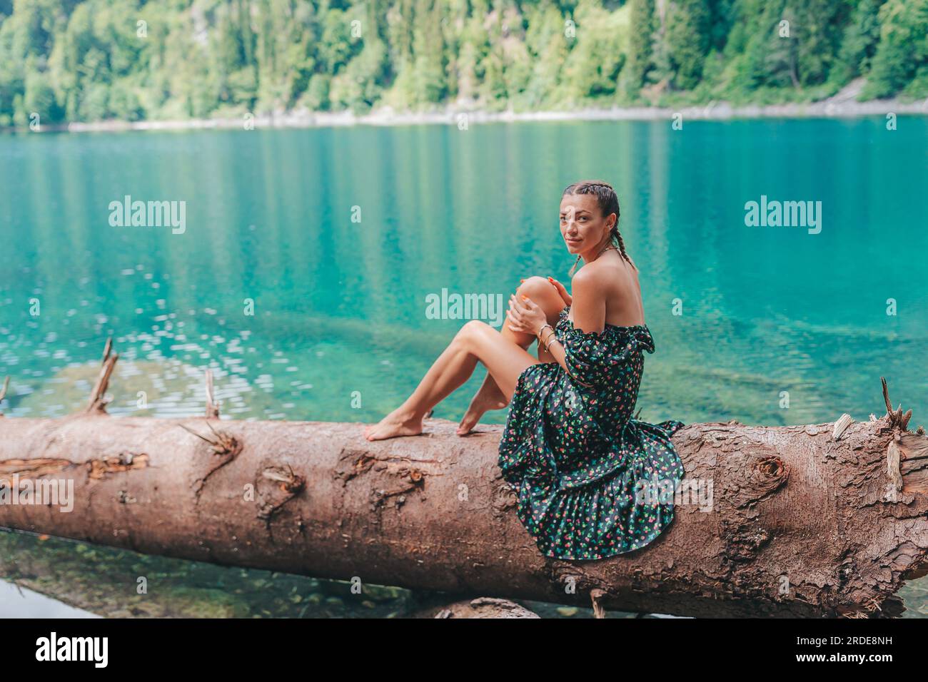 Happy romantic woman sitting by lake splashing water at perfect blue ...
