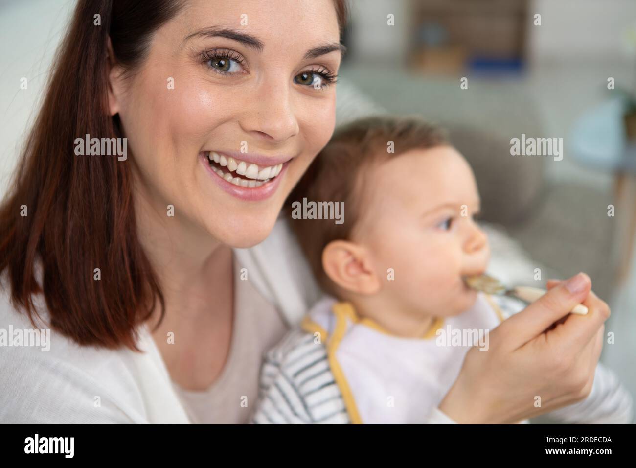 happy mum spoon feeding child son indoors Stock Photo - Alamy
