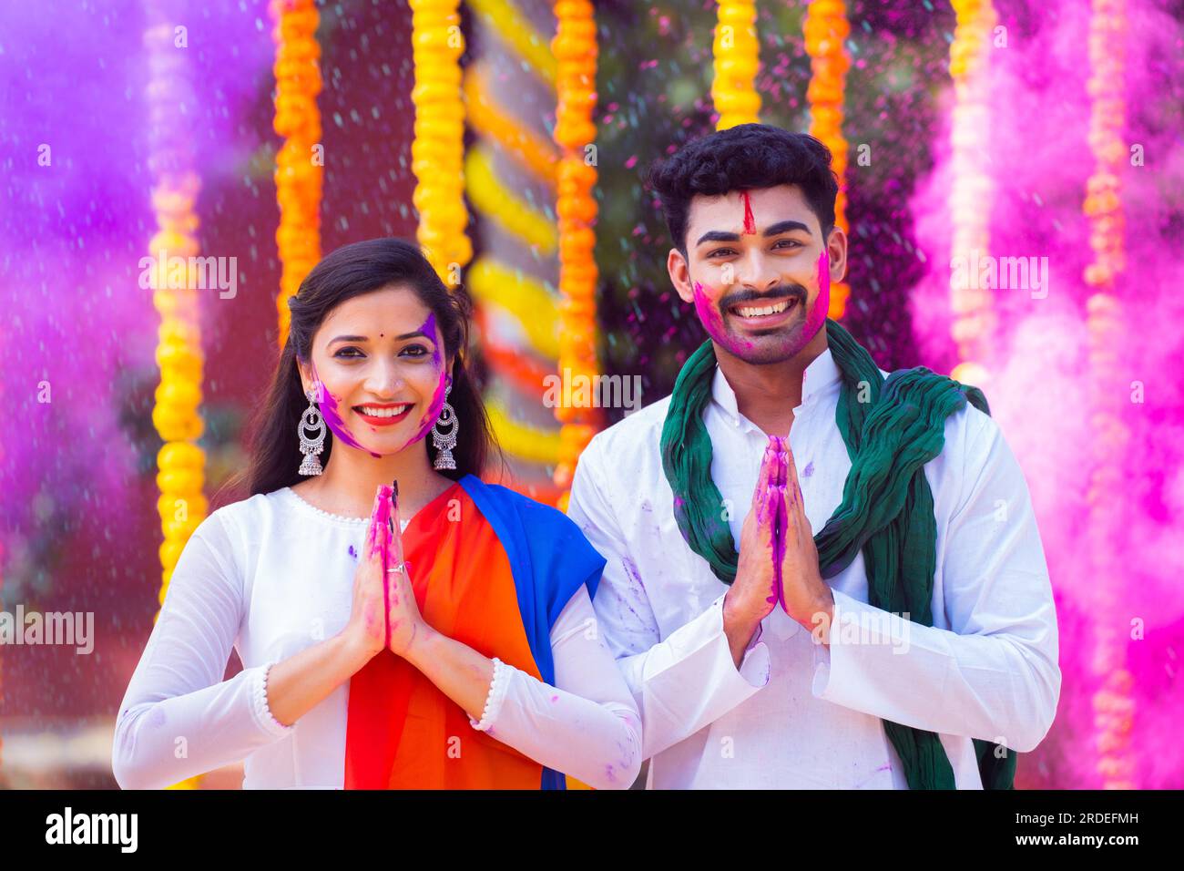 Happy young couple with color on face saying namaste againt flower ...