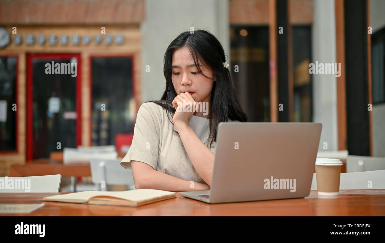 A thoughtful and focused Asian female freelancer working on her tasks ...
