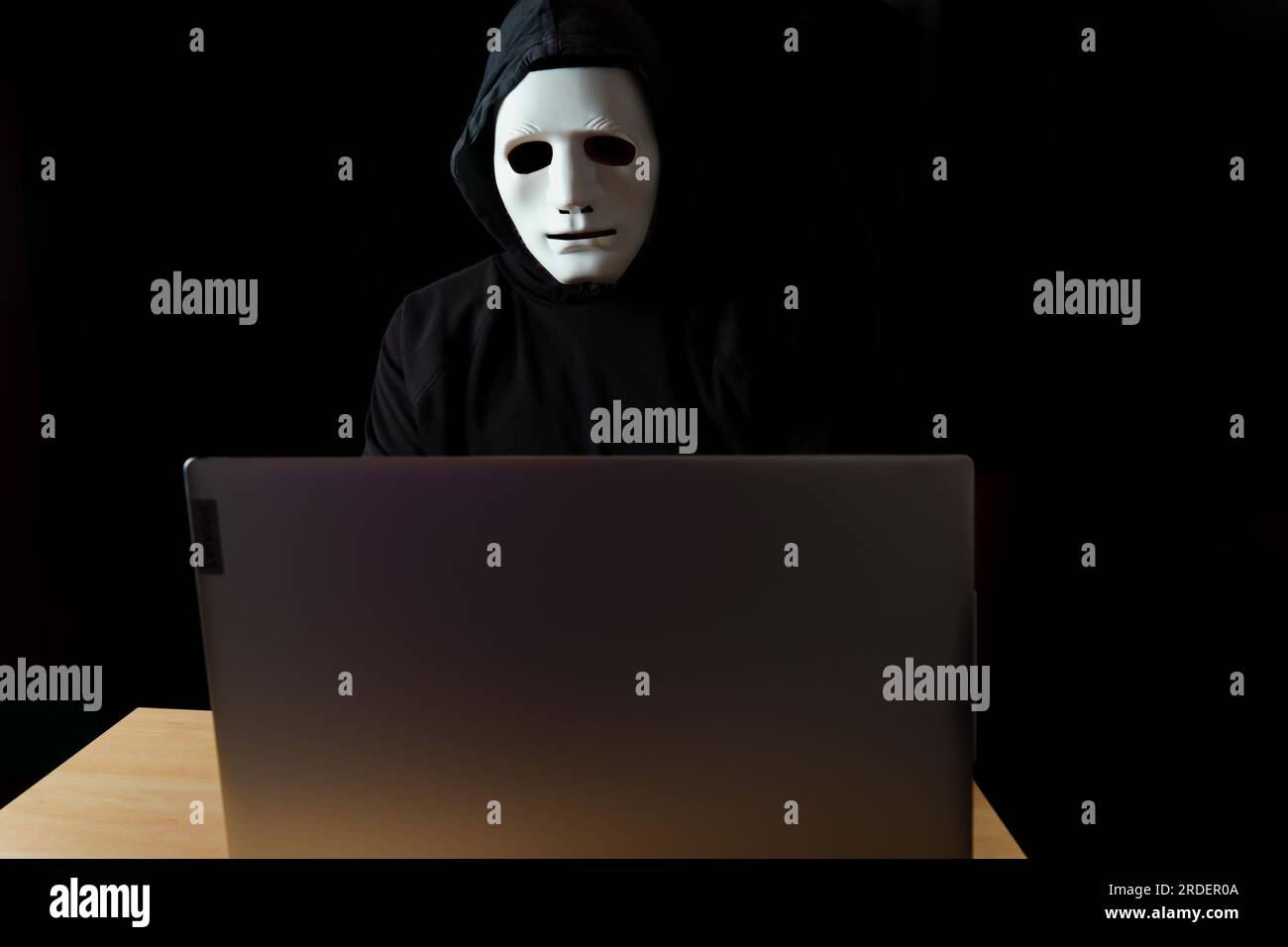 Male hacker dressed in black with a hood and a white mask behind a ...